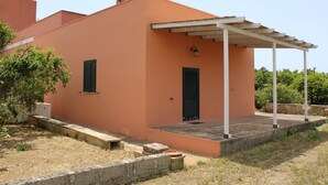 Um edifício de dois andares com telhado plano, um alpendre coberto e um pequeno jardim com uma árvore e um canteiro de flores.