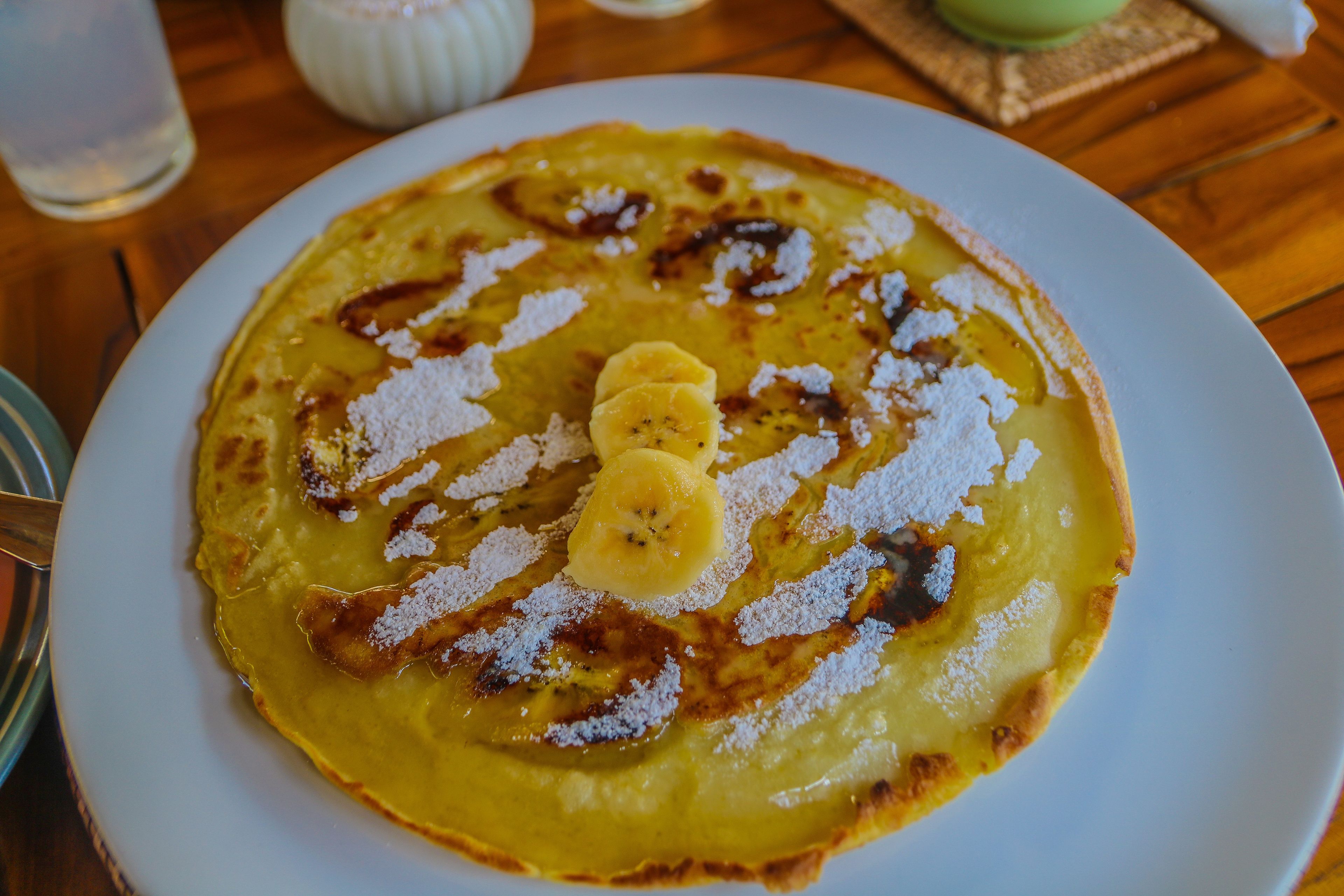 Um prato com uma crepe coberta com fatias de banana e açúcar em pó.
