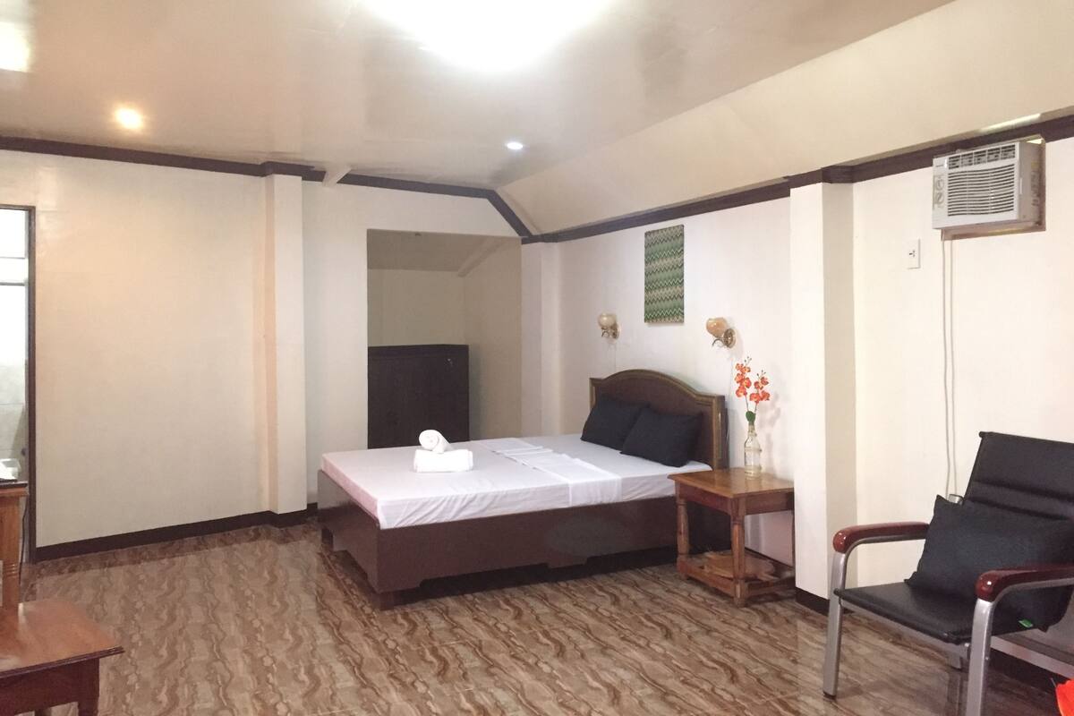 Quarto de hotel com uma cama, uma cadeira, uma mesa de cabeceira e um ar condicionado fixado na parede.