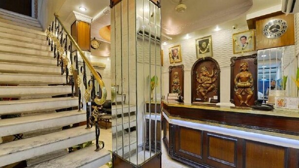 Uma escadaria com barreira de vidro, uma receção com estátuas e quadros nas paredes.