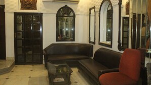 Uma sala de estar com um sofá de couro escuro, uma poltrona vermelha, uma mesa de centro de vidro e um espelho grande.