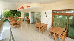Restaurante com decoração moderna, com mesas e cadeiras de madeira, divisória de vidro e placa sobre a entrada.