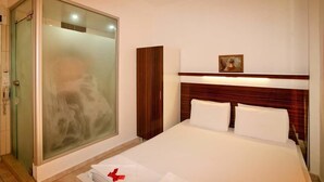 Quarto de hotel com cama, cabeceira de madeira, quadro e área de chuveiro com divisória de vidro.