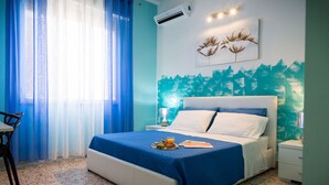 Quarto com cama, cadeira, mesa de cabeceira e parede com pintura floral.