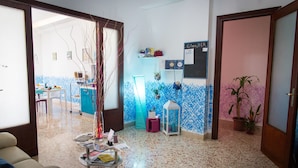 Uma sala de estar espaçosa com piso cerâmico, um sofá, uma mesa de centro com revistas e vista para a sala de jantar.