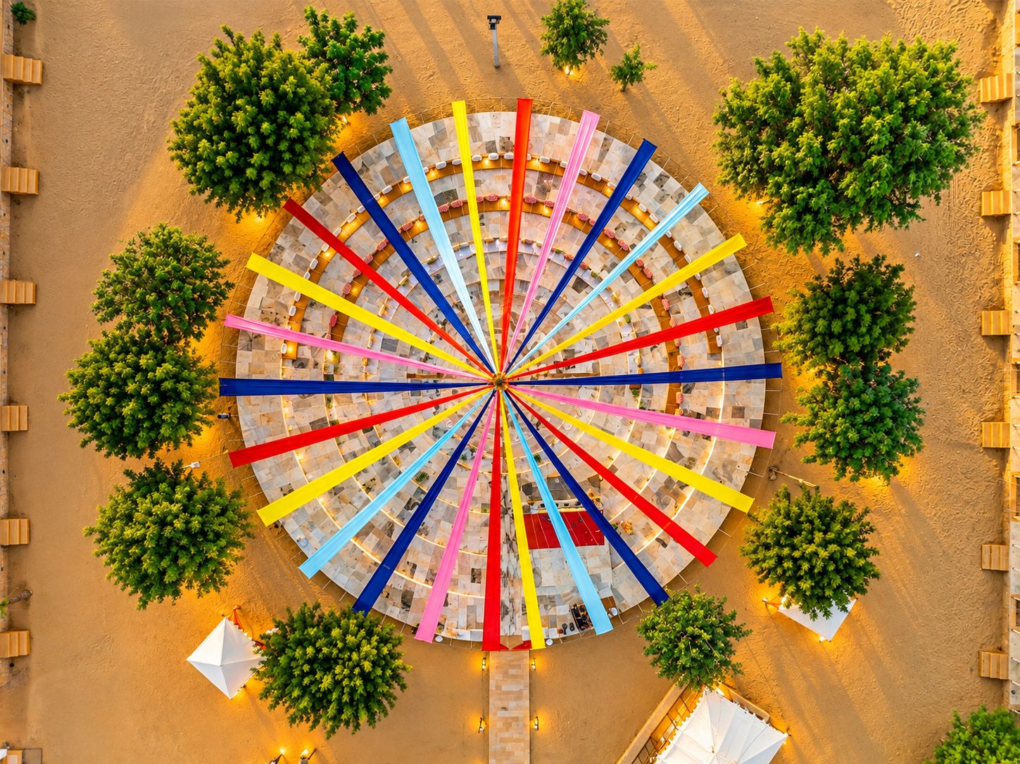 Área de estar externa circular com várias mesas e cadeiras, rodeada por árvores.