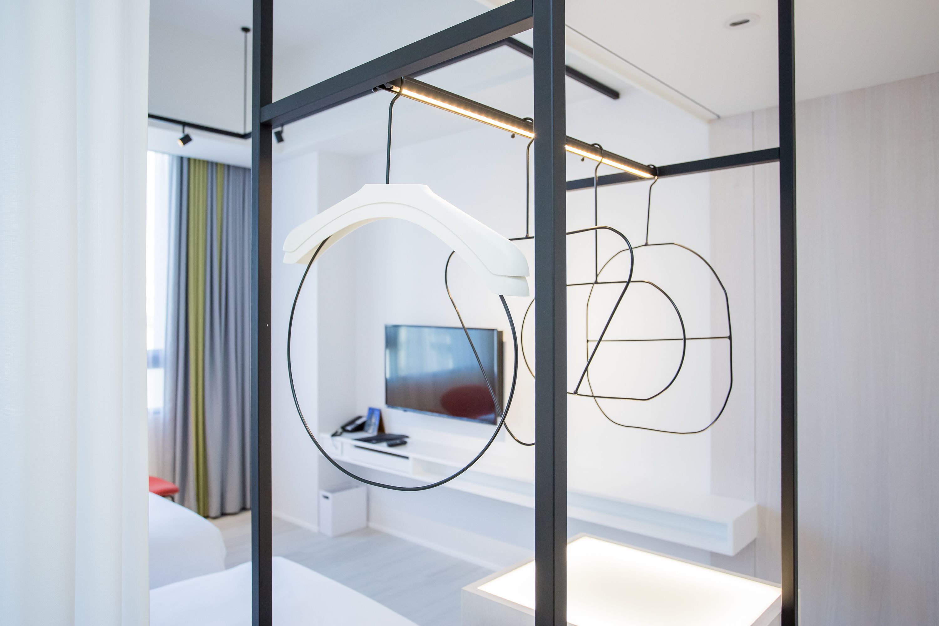Quarto de hotel moderno com design minimalista, apresentando uma grande TV de tela plana, um console branco e uma luminária pendente circular e peculiar.