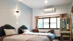 Quarto de hotel com duas camas, uma janela com cortinas, uma mesinha e uma cadeira.