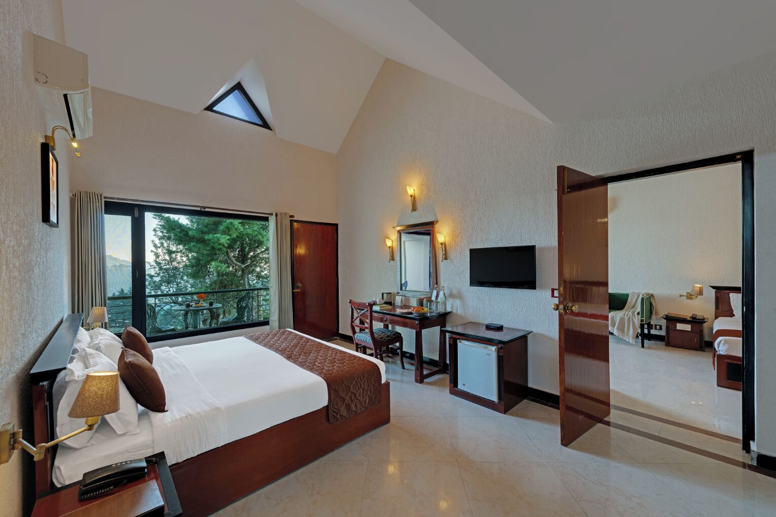Quarto de hotel moderno com uma cama grande, uma escrivaninha, uma TV e uma varanda com vista para árvores.