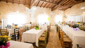 Uma sala de jantar com várias mesas e cadeiras, vigas de madeira no teto e aparelhos de ar condicionado nas paredes.