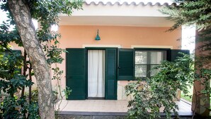 Um edifício com porta e persianas verdes, uma janela com cortina e uma pequena varanda.