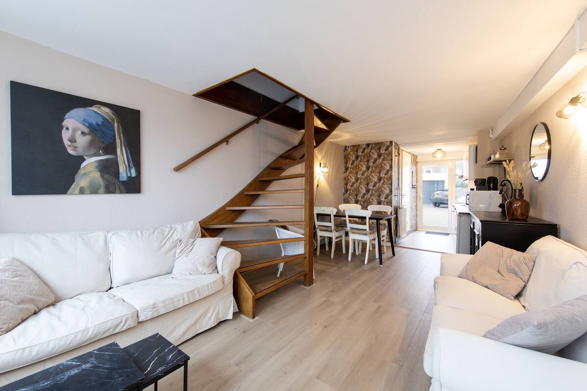 Uma sala de estar moderna com um sofá branco, uma escada de madeira e uma área de jantar.