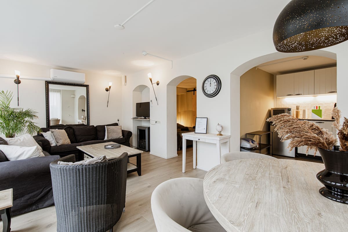 Uma sala de estar moderna com sofá, cadeiras, mesa de centro e mesa de jantar. Há uma área de cozinha com armários e micro-ondas.