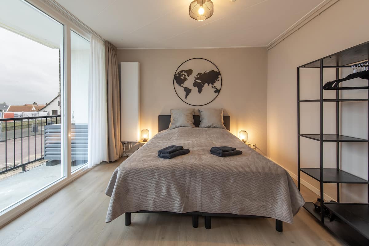 Quarto com cama grande, mapa-múndi na parede, guarda-roupa e vista para o exterior.