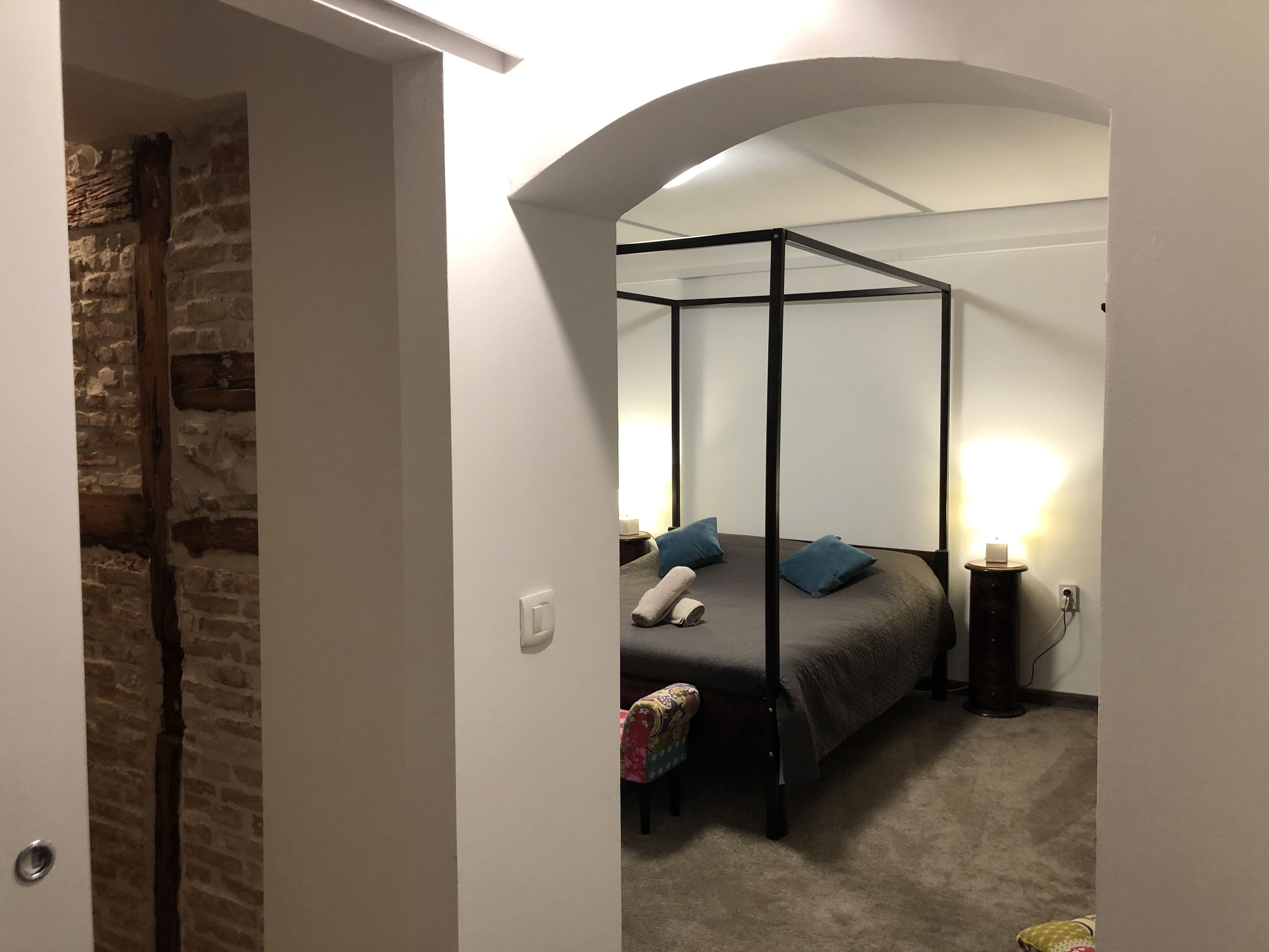 Quarto com uma cama de dossel, uma pequena mesa de cabeceira e uma cadeira.