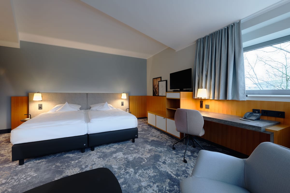 Quarto de hotel com cama de casal, uma escrivaninha com computador, uma cadeira e uma televisão.