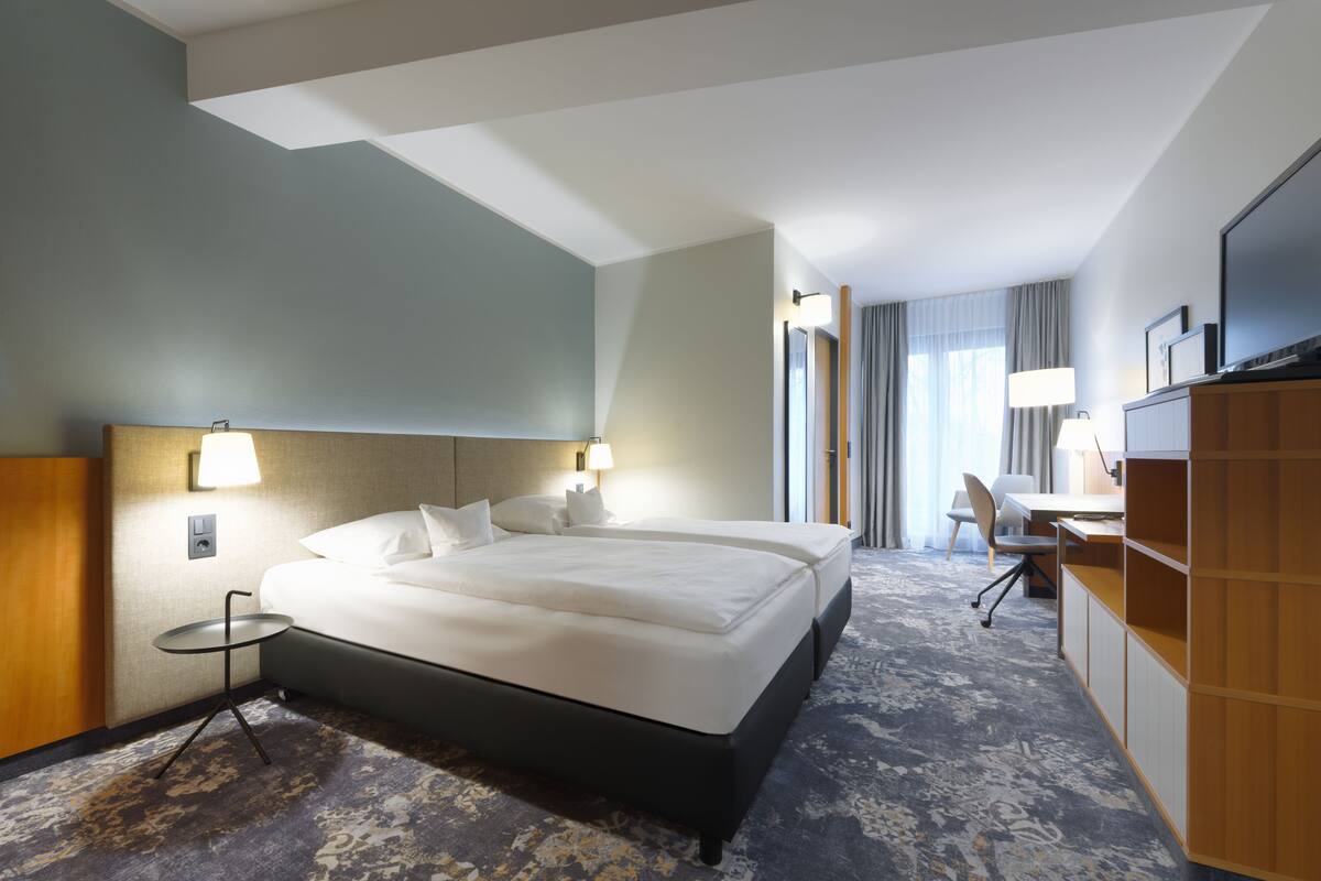 Quarto de hotel com uma cama grande, mesas de cabeceira, uma escrivaninha e uma televisão.