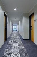 Um corredor com carpete estampado, paredes brancas e portas de ambos os lados.