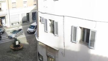 Rua estreita com um edifício branco, com várias janelas com persianas, uma fachada visível e calçada de pedra.