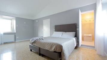 Quarto com cama, mesa de cabeceira, guarda-roupa e banheiro visível por uma porta aberta.