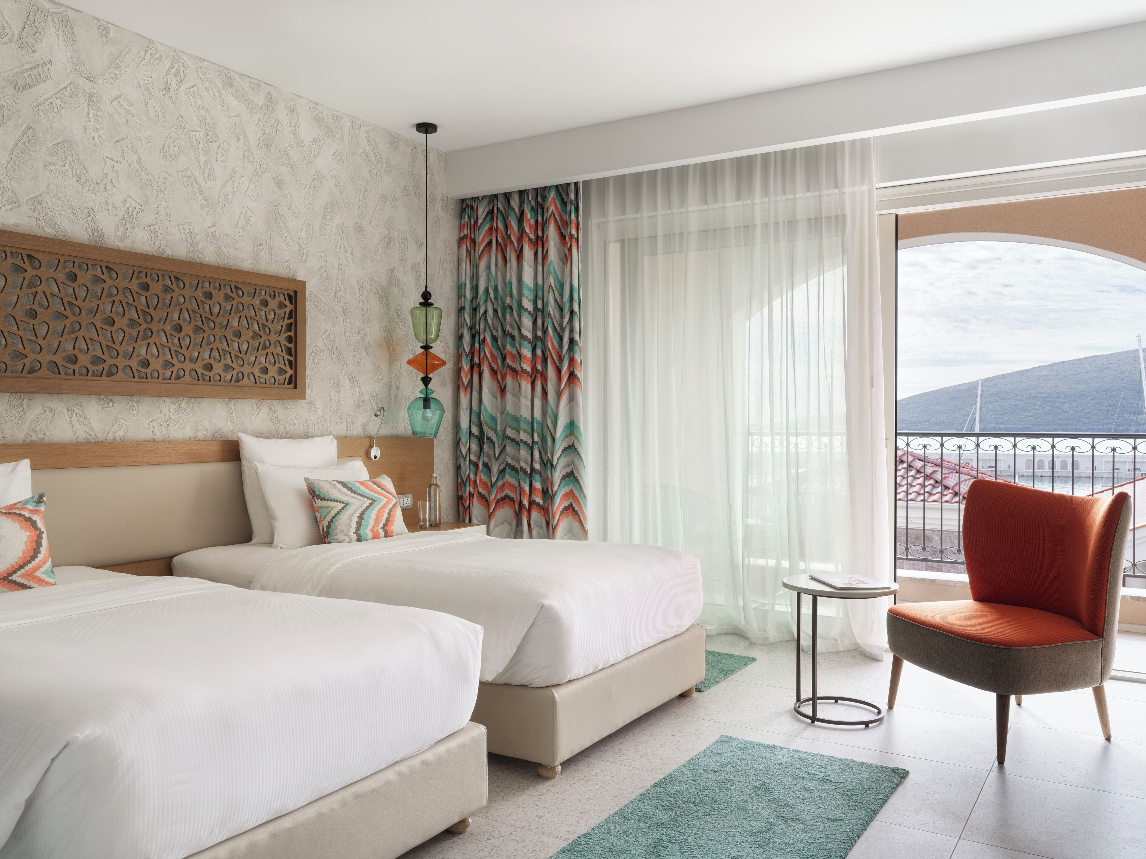 Quarto de hotel com duas camas, vista para o mar e varanda com guarda-corpo.