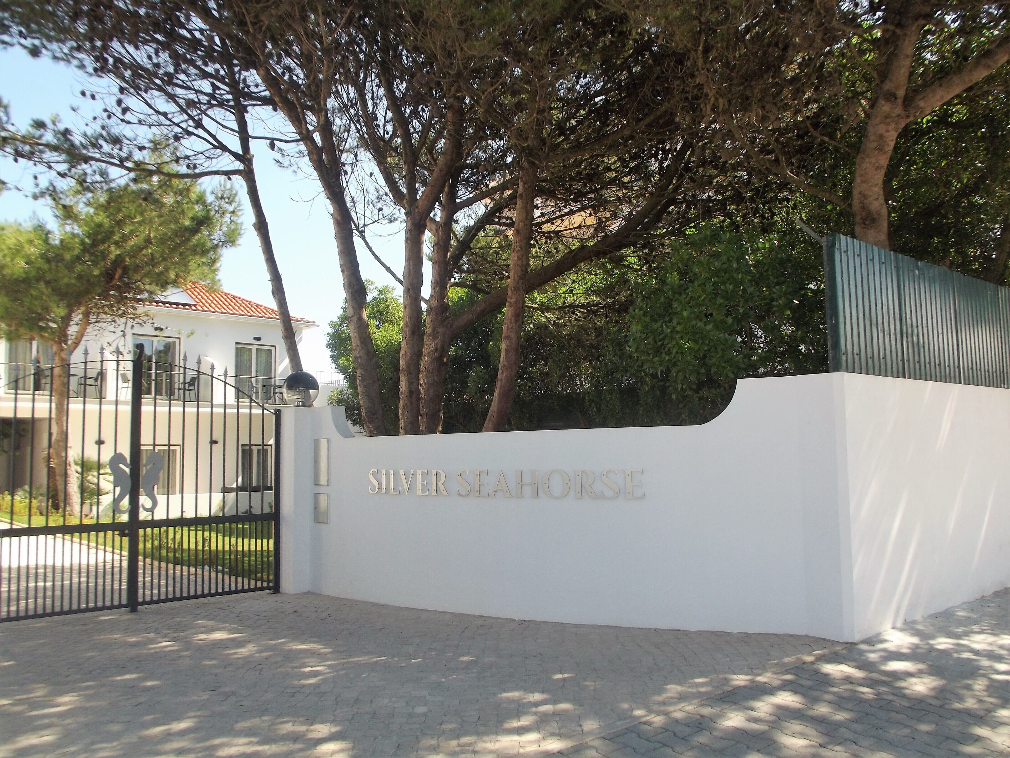Uma entrada com portão e uma placa com a inscrição "SILVER SEAHORSE", com um edifício branco ao fundo.