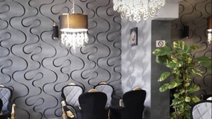 Uma sala de jantar com cadeiras estofadas pretas, uma mesa de vidro e um candelabro.