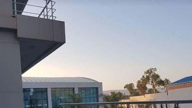 Um edifício moderno com fachada de vidro, área de estar externa e vista para carros estacionados e árvores.