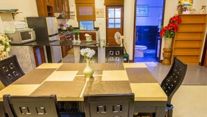 Uma área de refeições com mesa e cadeiras xadrez, um vaso com flores e uma cozinha ao fundo.