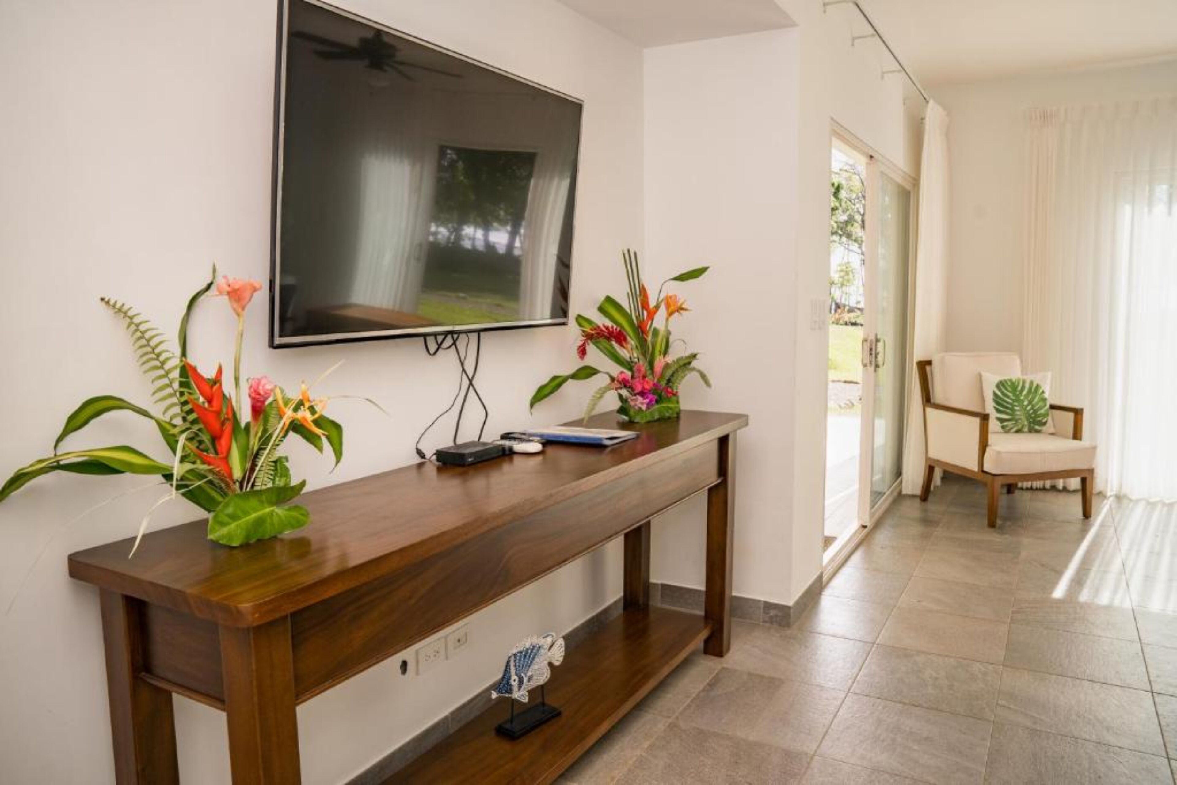 Uma sala de estar moderna com uma mesa consola de madeira, uma TV de tela plana na parede e dois arranjos de flores.
