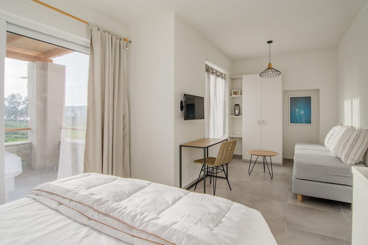 Quarto de hotel com cama, escrivaninha, poltrona, sofá e televisão.