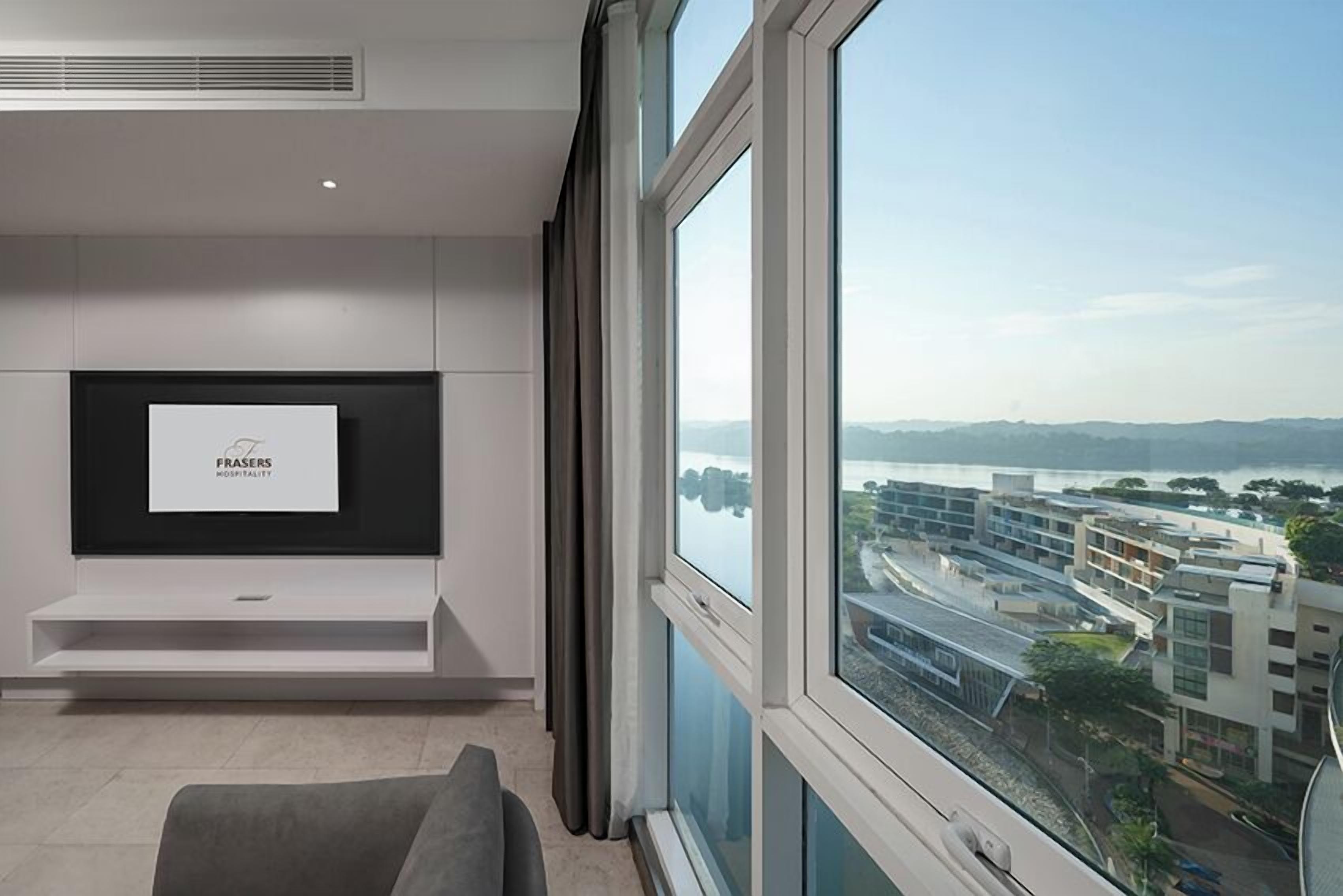 Quarto de hotel moderno com uma grande janela que oferece vista para a cidade e para o mar.