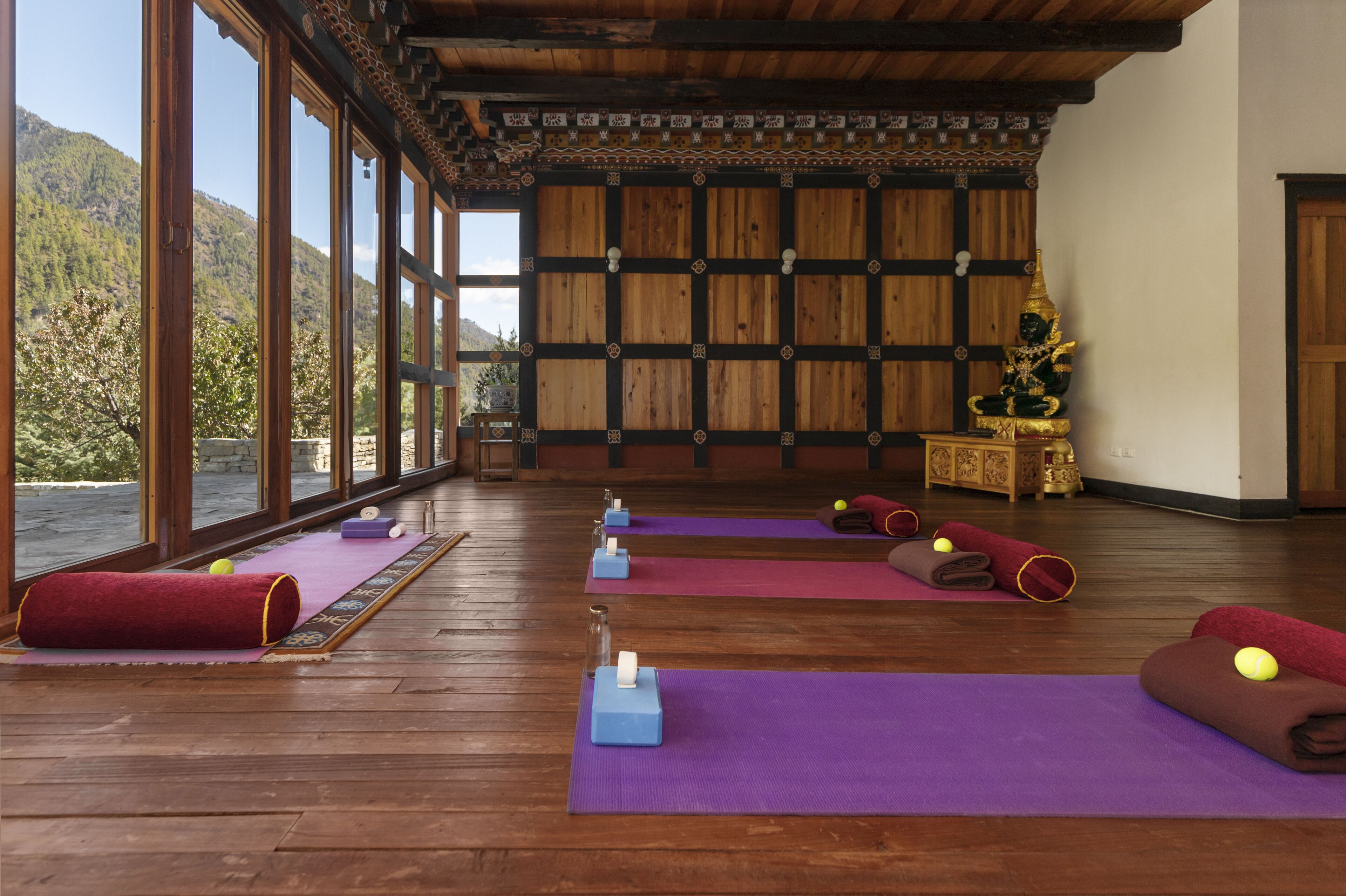 Um estúdio de yoga com piso de madeira, tapetes roxos e vista para uma montanha.