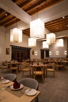 Uma ampla área de refeições com mesas e cadeiras de madeira, grandes luminárias pendentes e teto de madeira tradicional.