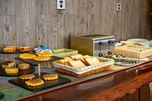 Buffet com diversos pães e doces à mostra.