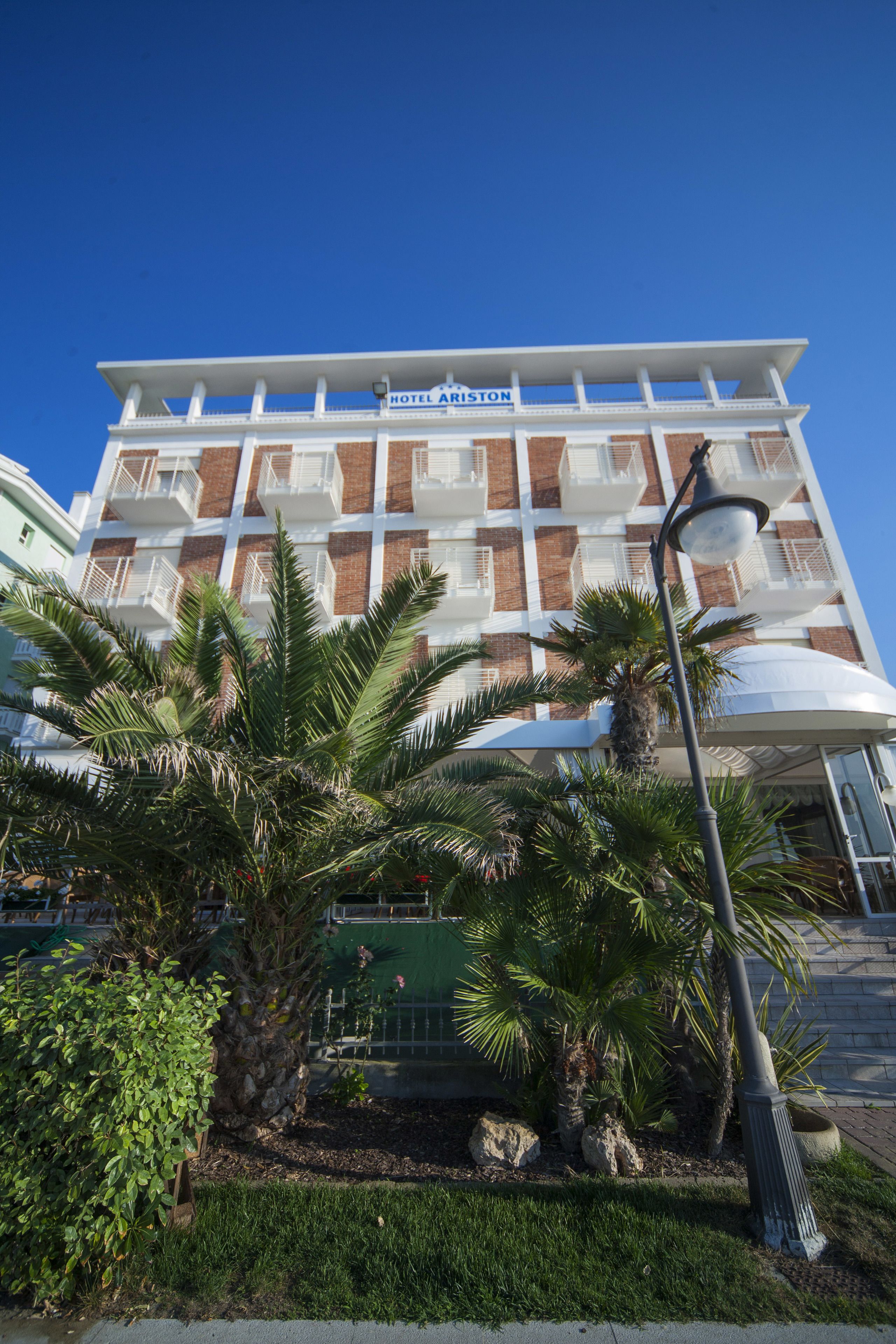 Um hotel com fachada branca, várias varandas e uma placa indicando "HOTEL ARISTON".