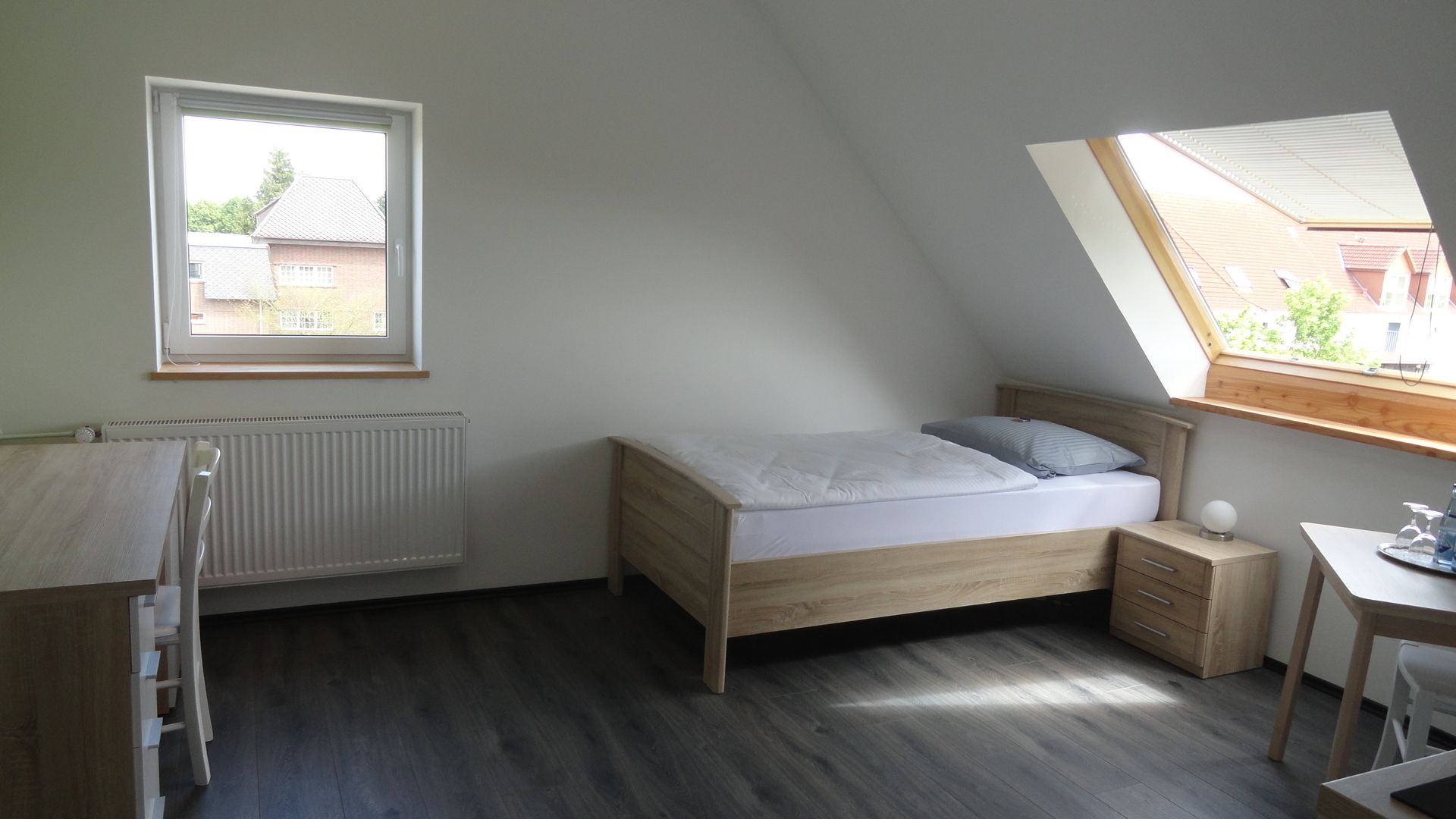 Um quarto com teto inclinado, uma cama, uma escrivaninha e um radiador.