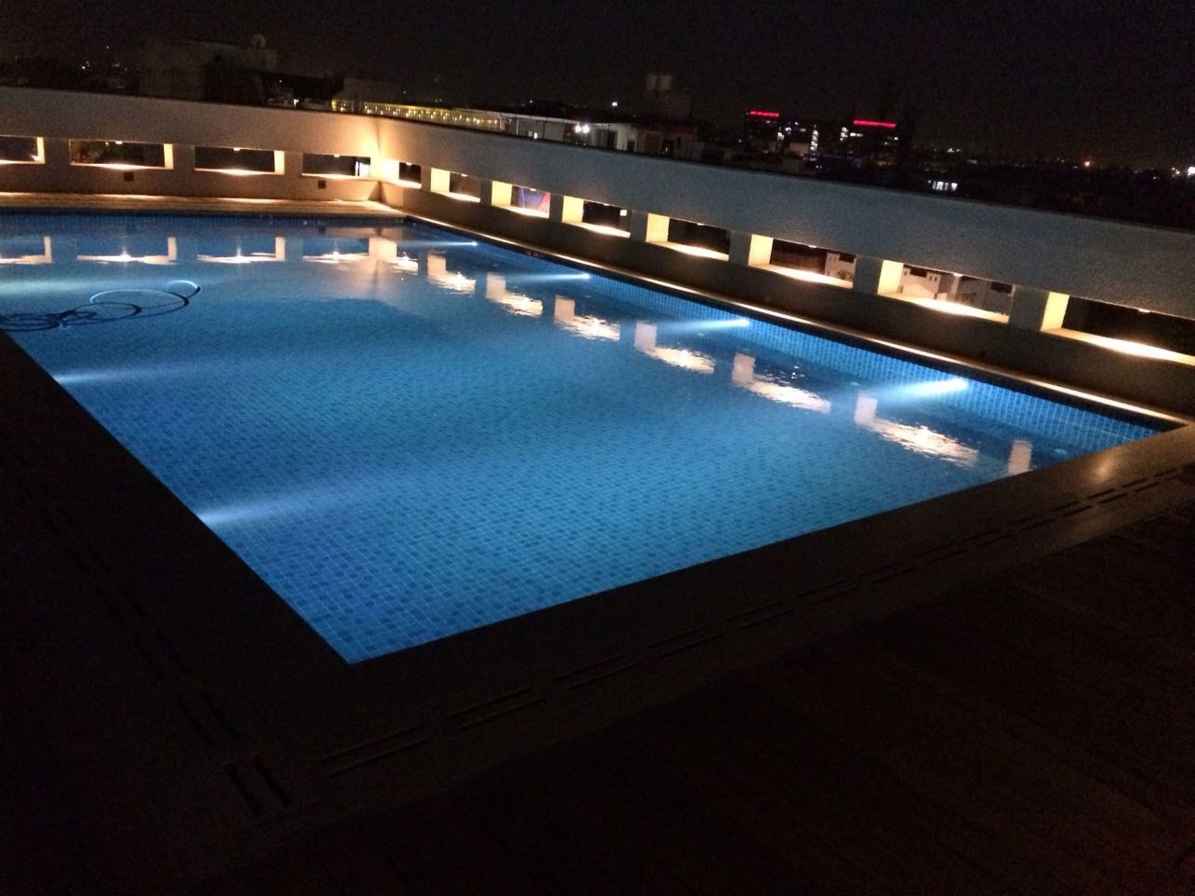 Piscina com deck revestido e bordas iluminadas, cercada por um muro baixo.