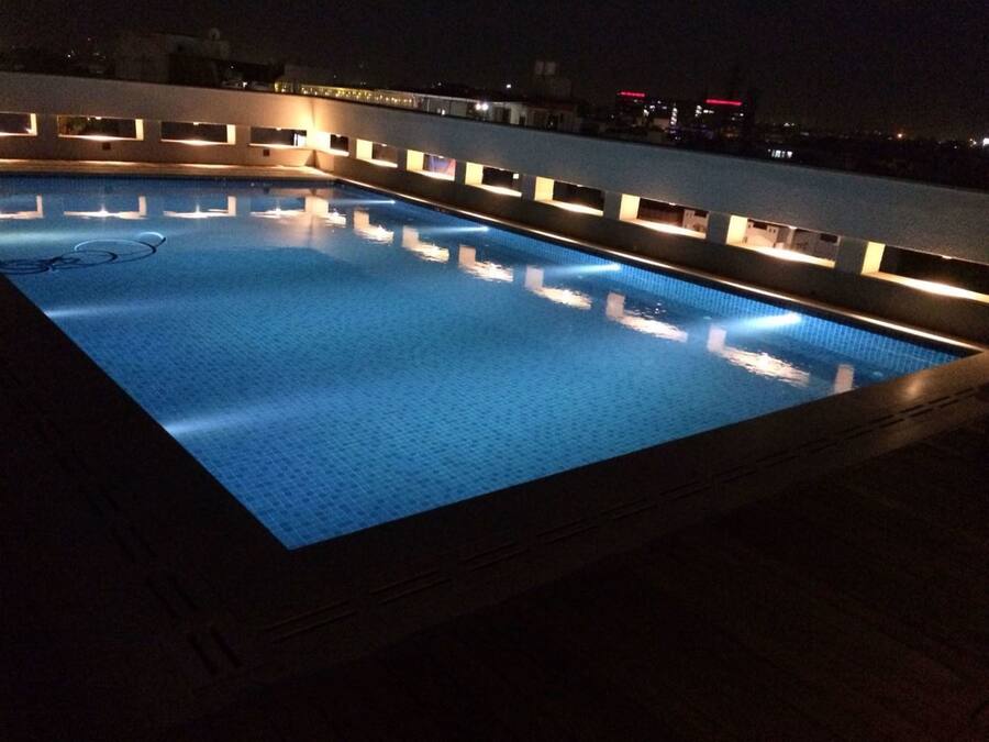 Piscina com deck revestido e bordas iluminadas, cercada por um muro baixo.