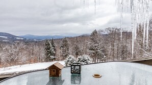 Vista de um quarto com uma grande janela para uma paisagem nevada com árvores e montanhas.