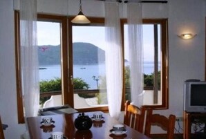 Um quarto com uma mesa de madeira, uma televisão e amplas janelas com cortinas.