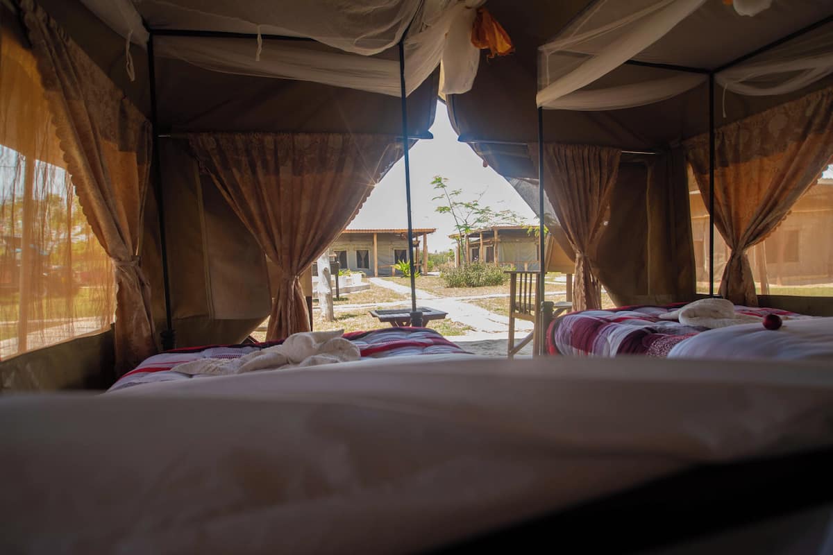 Alojamento tipo tenda com duas camas, uma mesa e vista para edifícios ao longe.