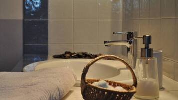 Uma casa de banho com uma banheira branca, uma torneira prateada, um dispensador de sabonete de vidro transparente e uma cesta de tecido com uma toalha.