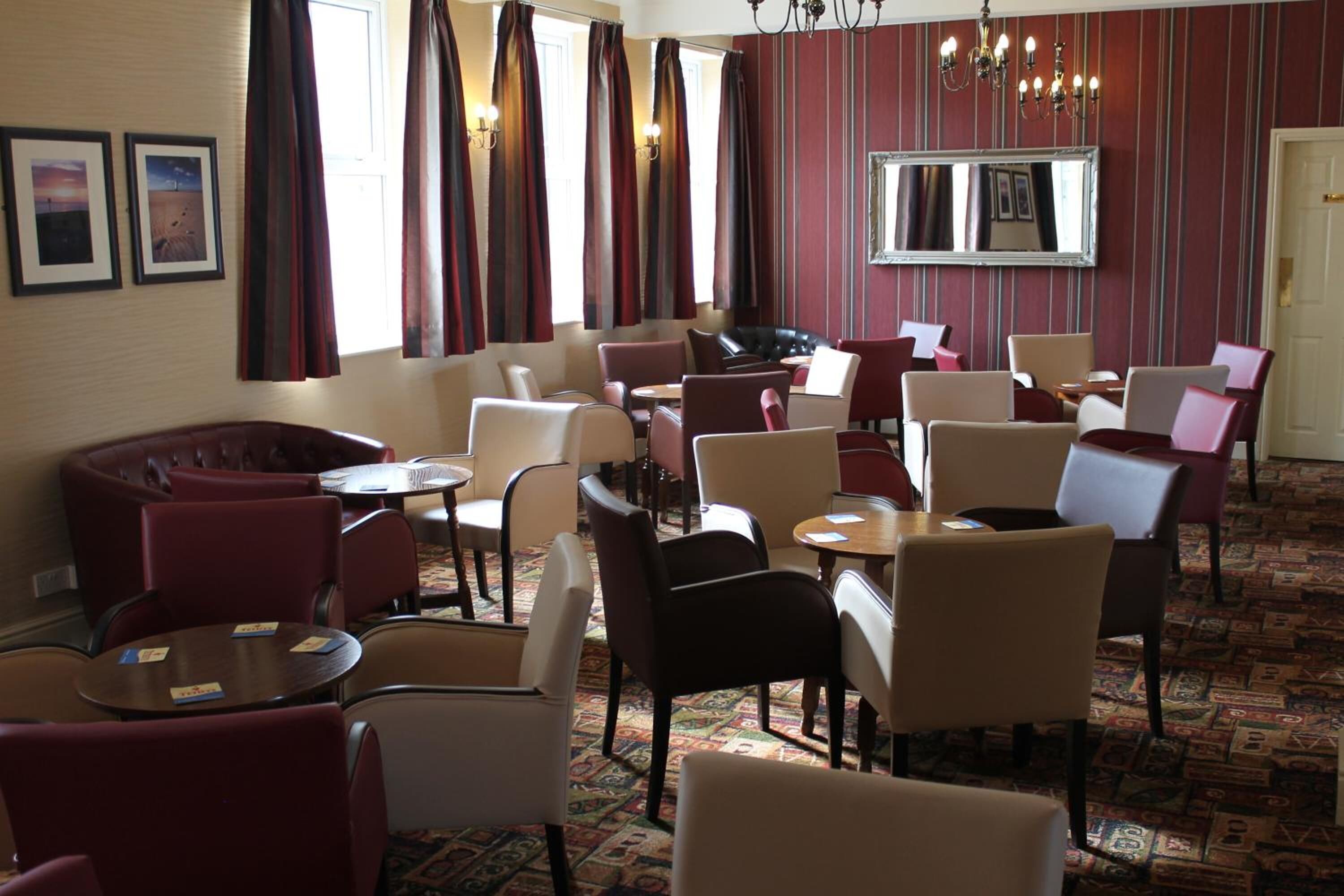 Um hall de hotel com várias áreas de estar, incluindo mesas redondas e cadeiras, e um espelho grande na parede.