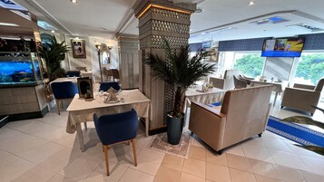 Restaurante com mesa de bilhar, cadeiras azuis e uma grande planta em vaso.