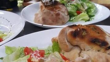 Mesa de jantar com pratos de comida, incluindo frango grelhado e saladas.
