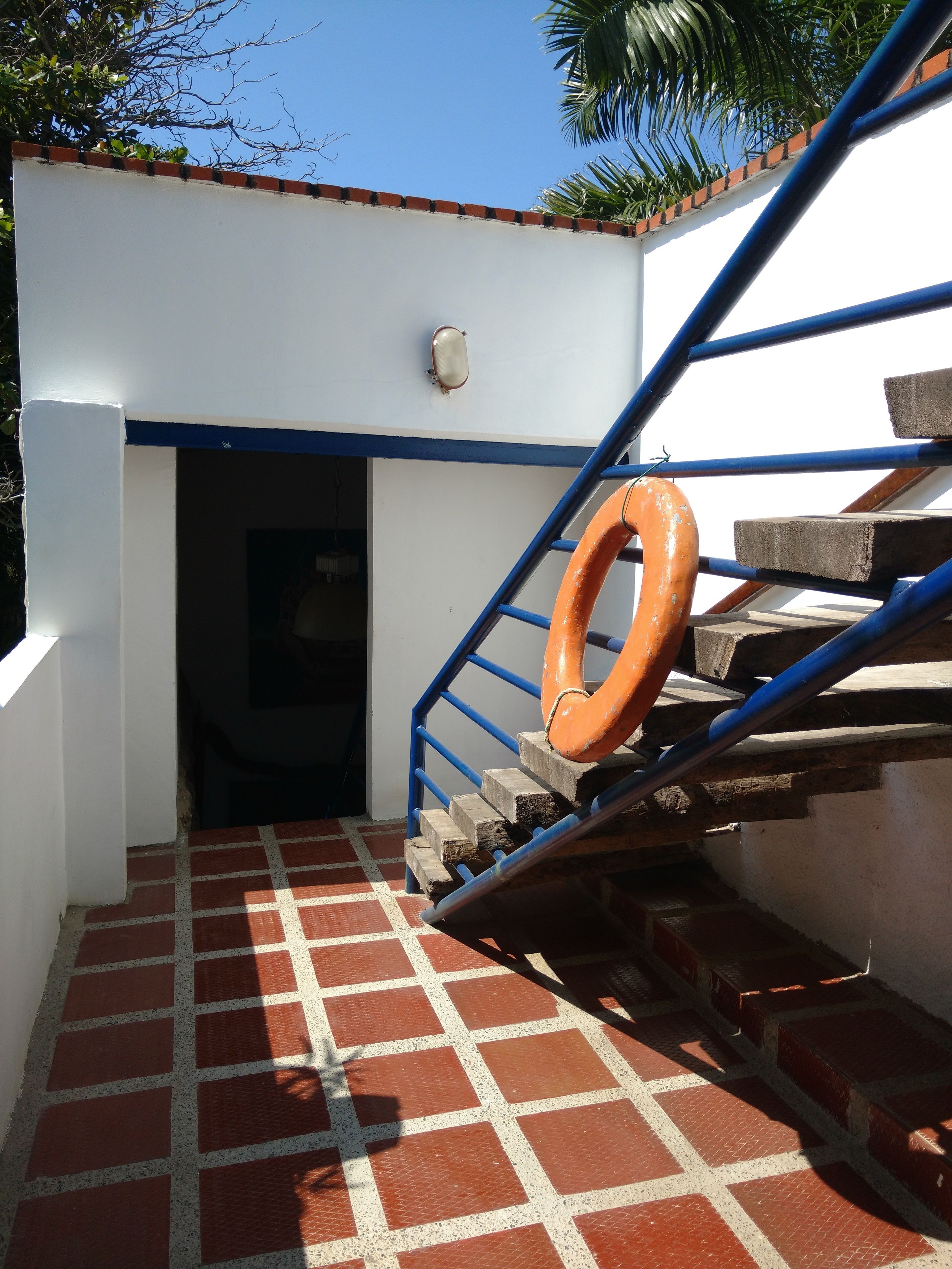 Uma escadaria com corrimãos azuis que leva a uma porta, um salva-vidas pendurado no corrimão e um chão de azulejos.