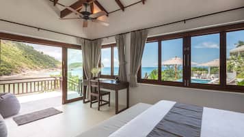 Quarto com cama grande, escrivaninha e vista para o oceano.