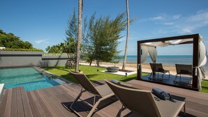 Uma área à beira da piscina com espreguiçadeiras, um pérgola com tecido pendurado e vista para o oceano.