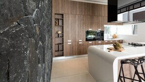 Uma cozinha moderna com ilha central, armários de madeira e parede decorativa em pedra.